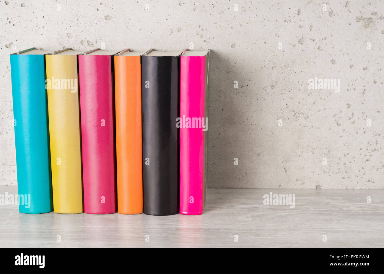 Books of different colors are on the shelf, concrete wall background ...