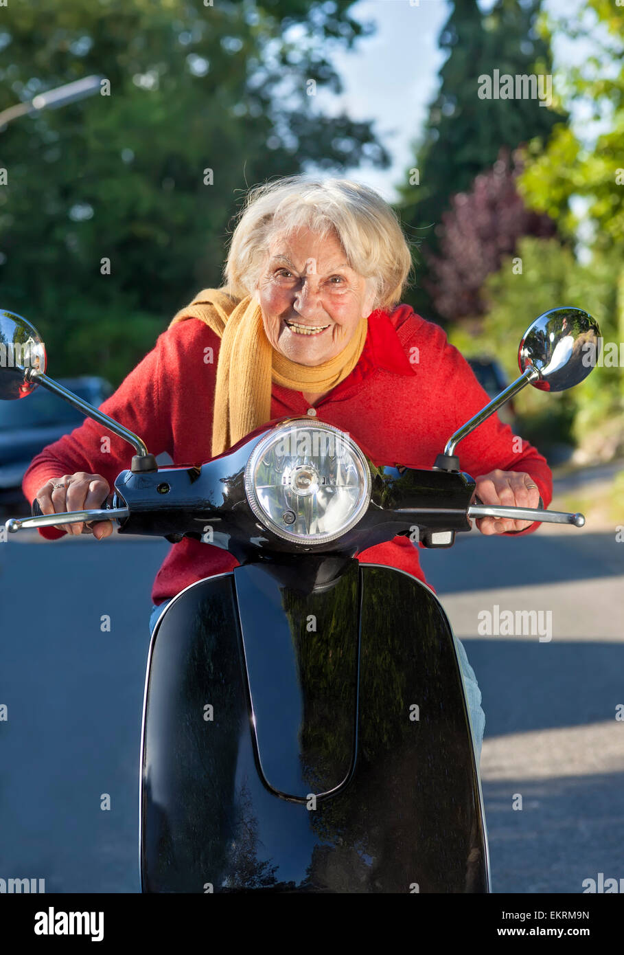 Elderly lady having fun on her scooter crouching low of the handlebars ...