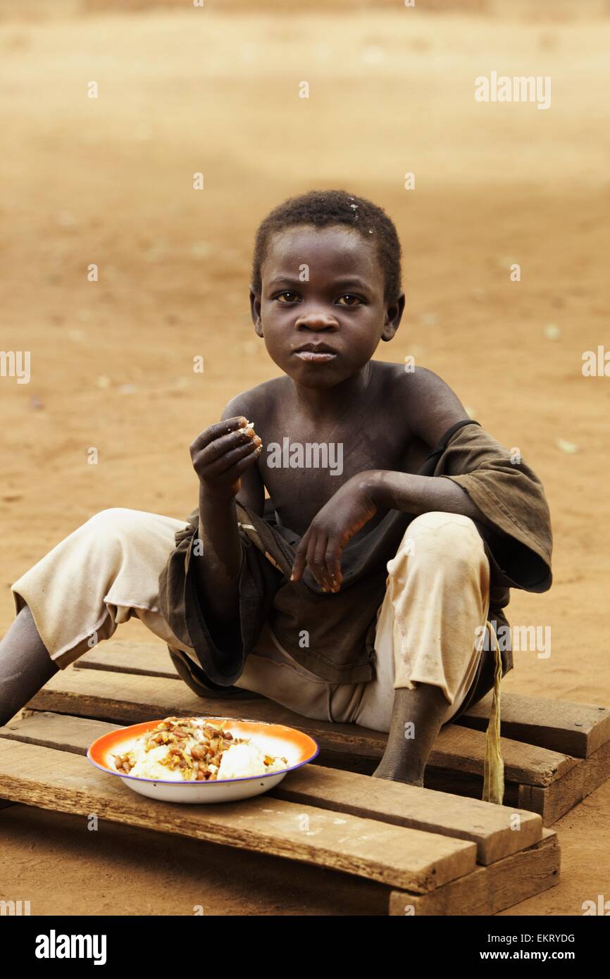 A Boy Eats A Meal Sitting On Boards On The Ground; Manica, Mozambique ...