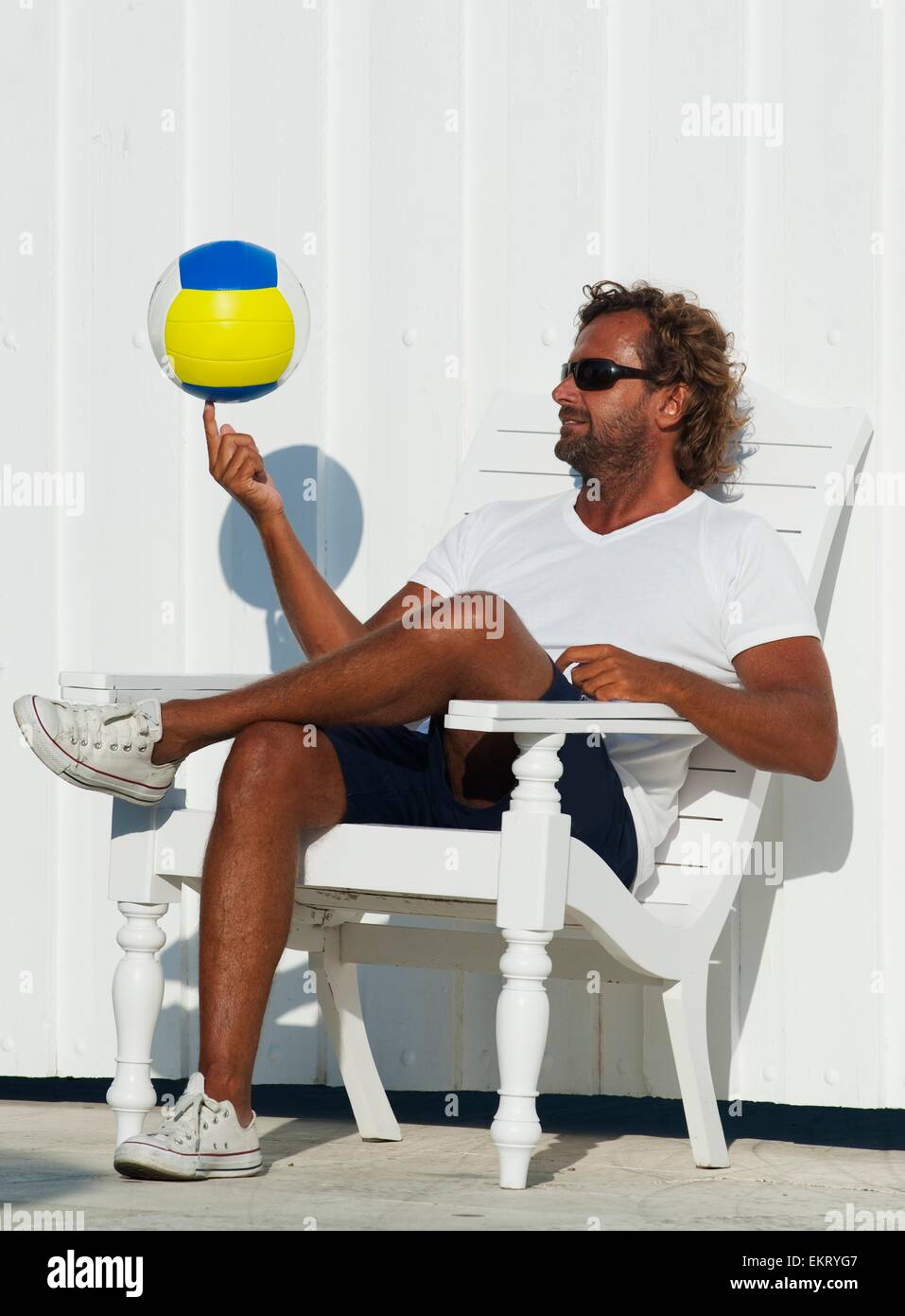 A Man Balancing A Ball On His Finger While Sitting In A Deck Chair At ...