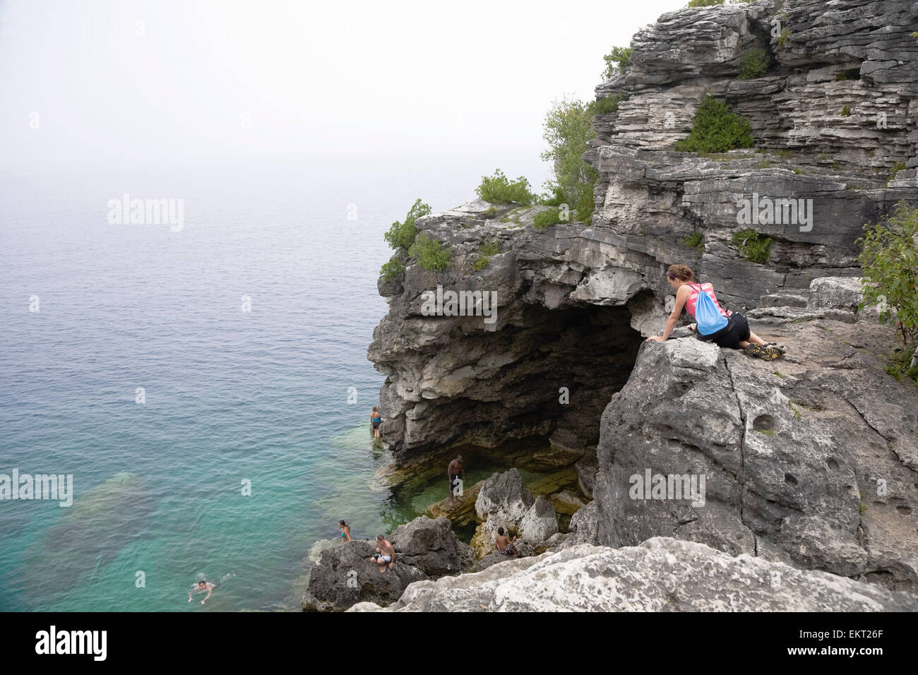 Young woman looking over cliff to swimmers below in Bruce Peninsula ...