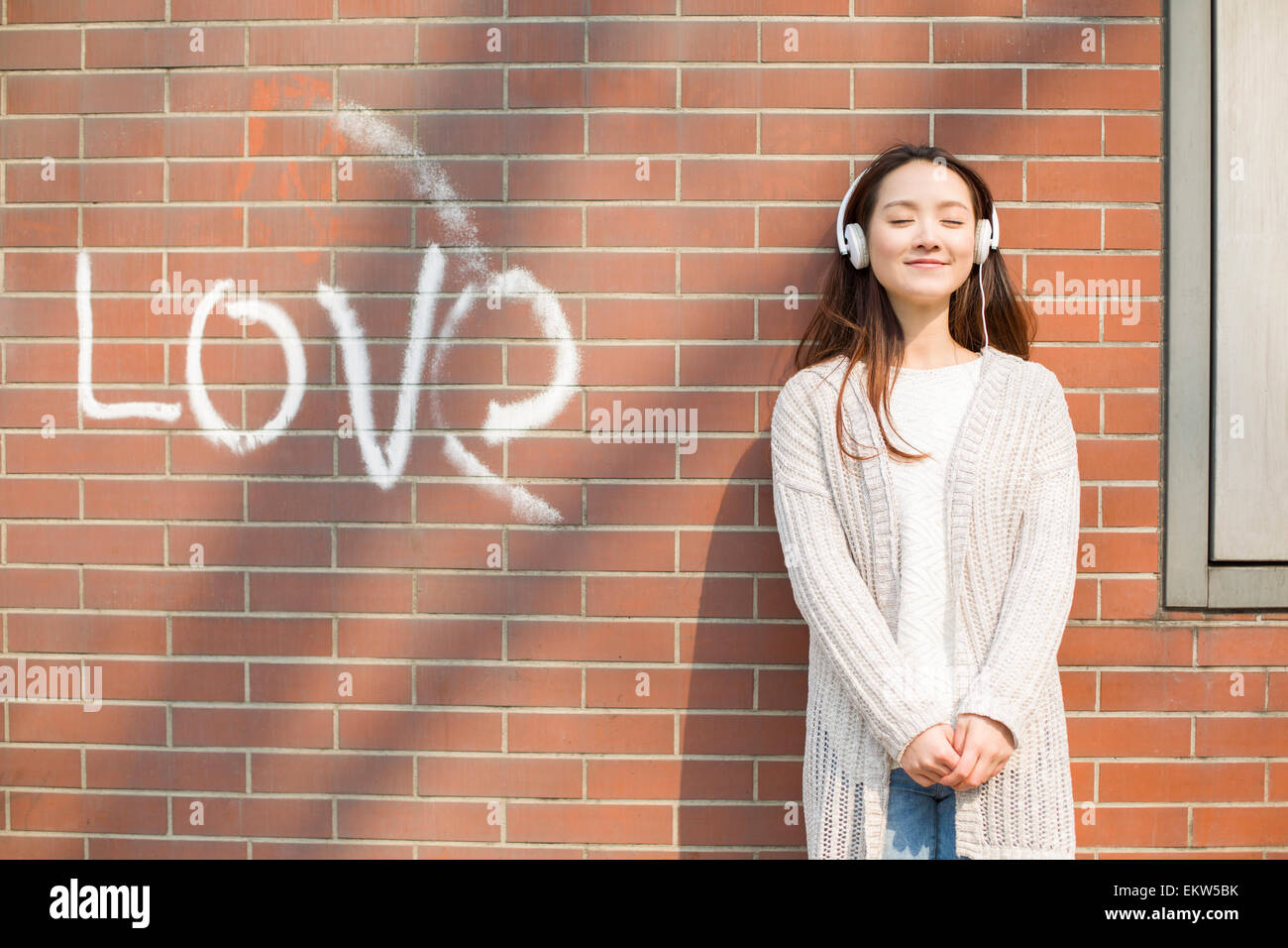 Young woman leaning against wall listening to music Stock Photo - Alamy