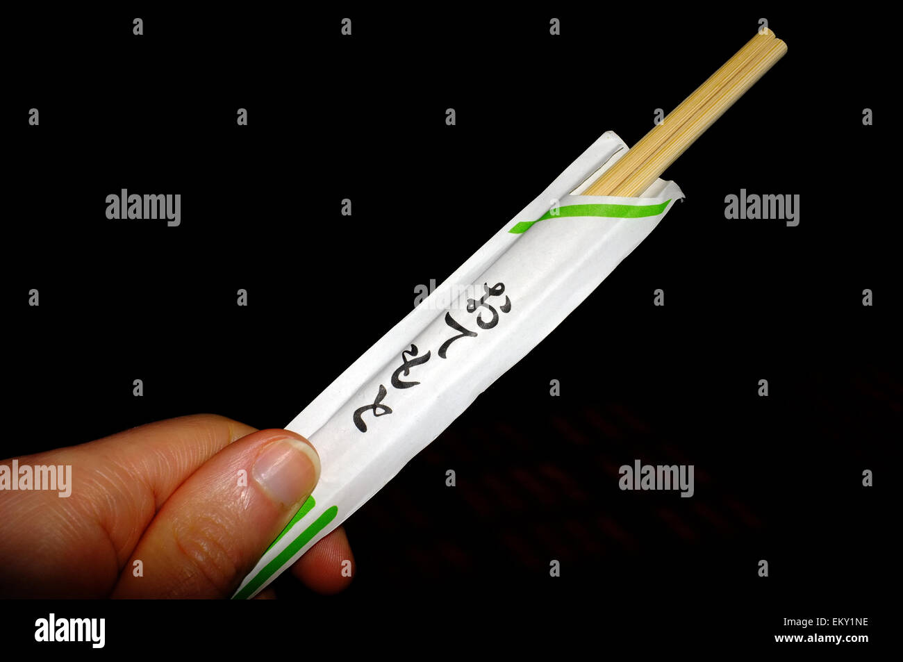 A white hand holding a packet of unopened chopsticks against a black ...