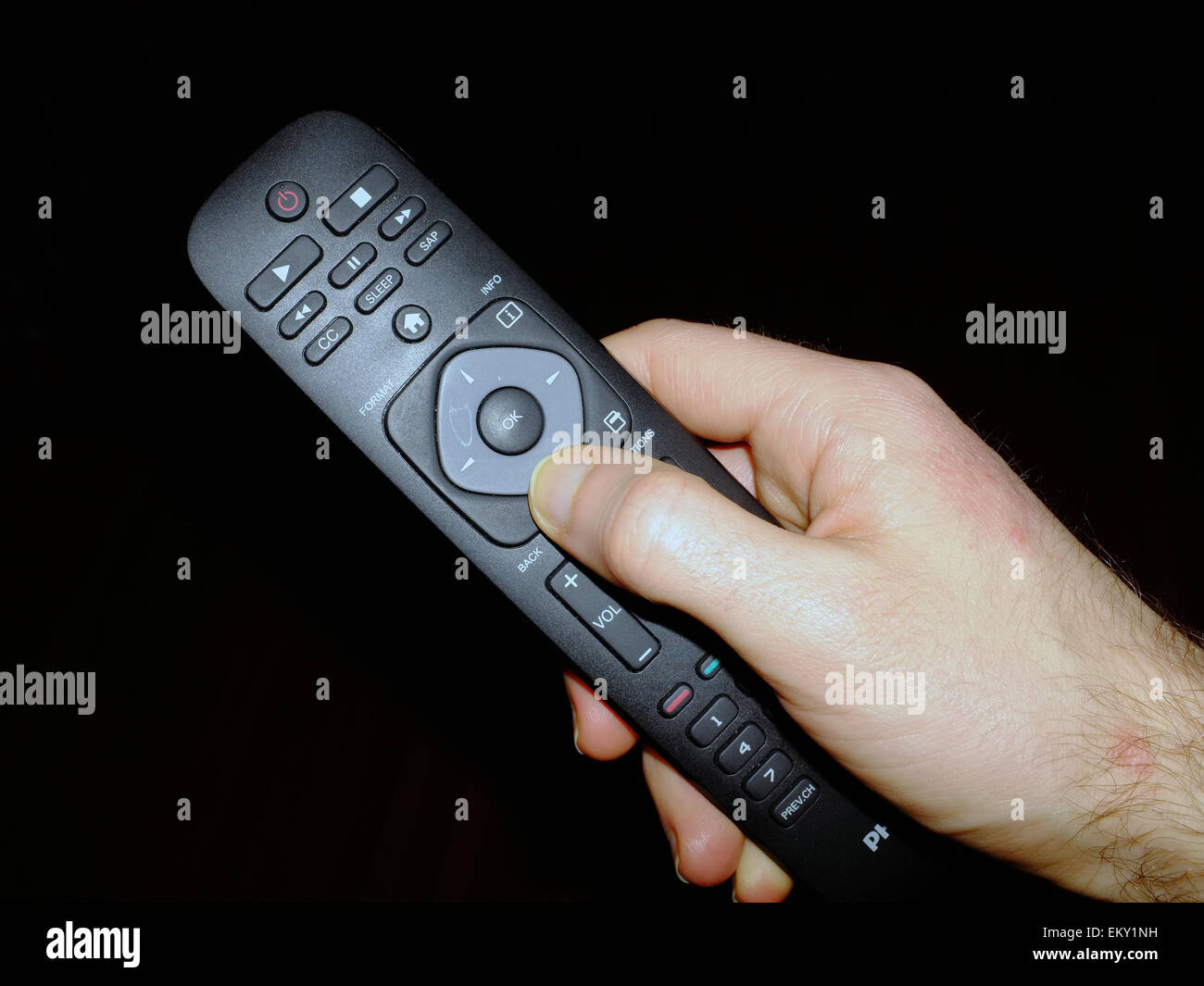 A white hand holding a television controller dice against a black ...