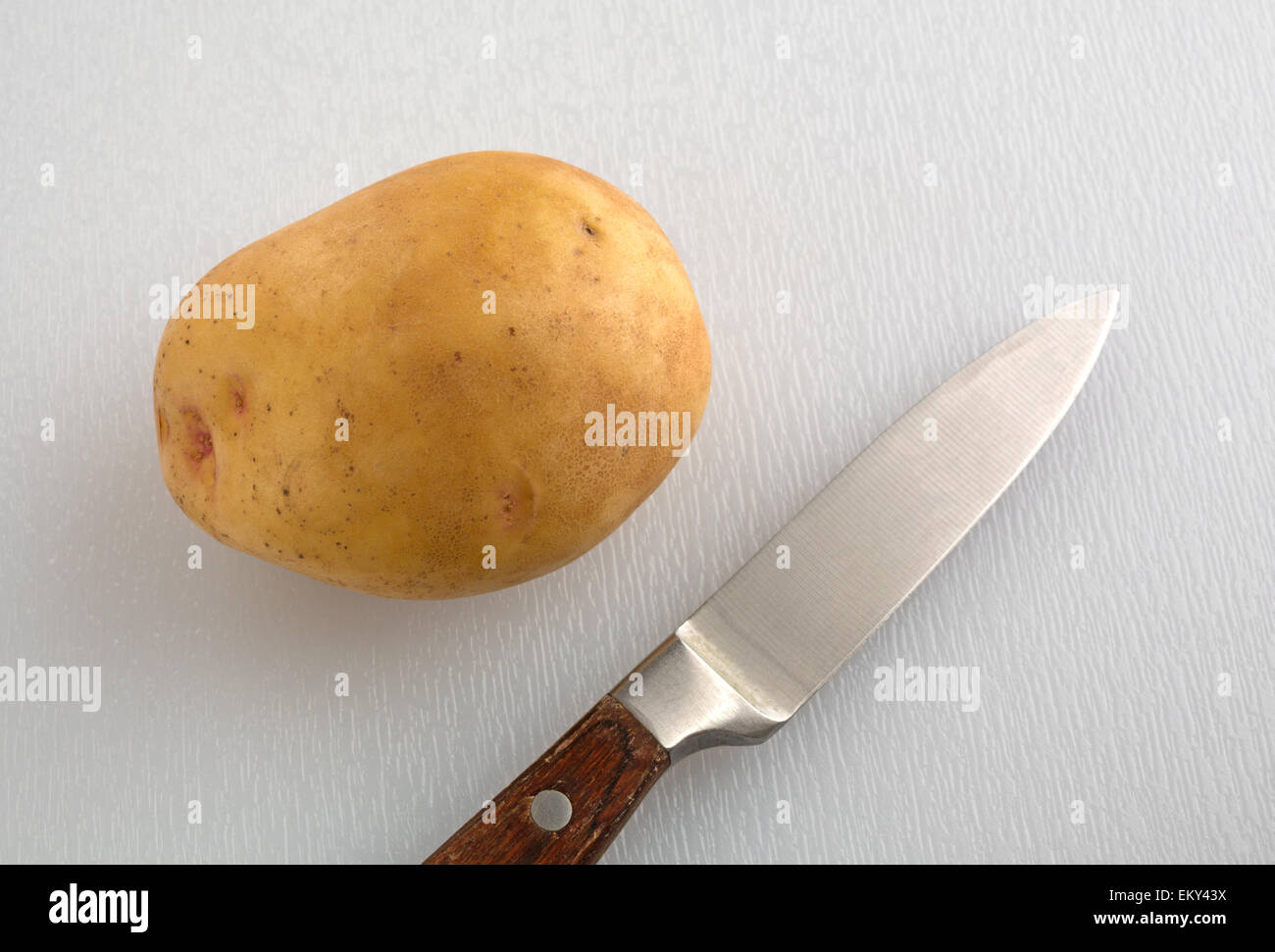 A single yellow gold potato on a plastic cutting board with a sharp old ...