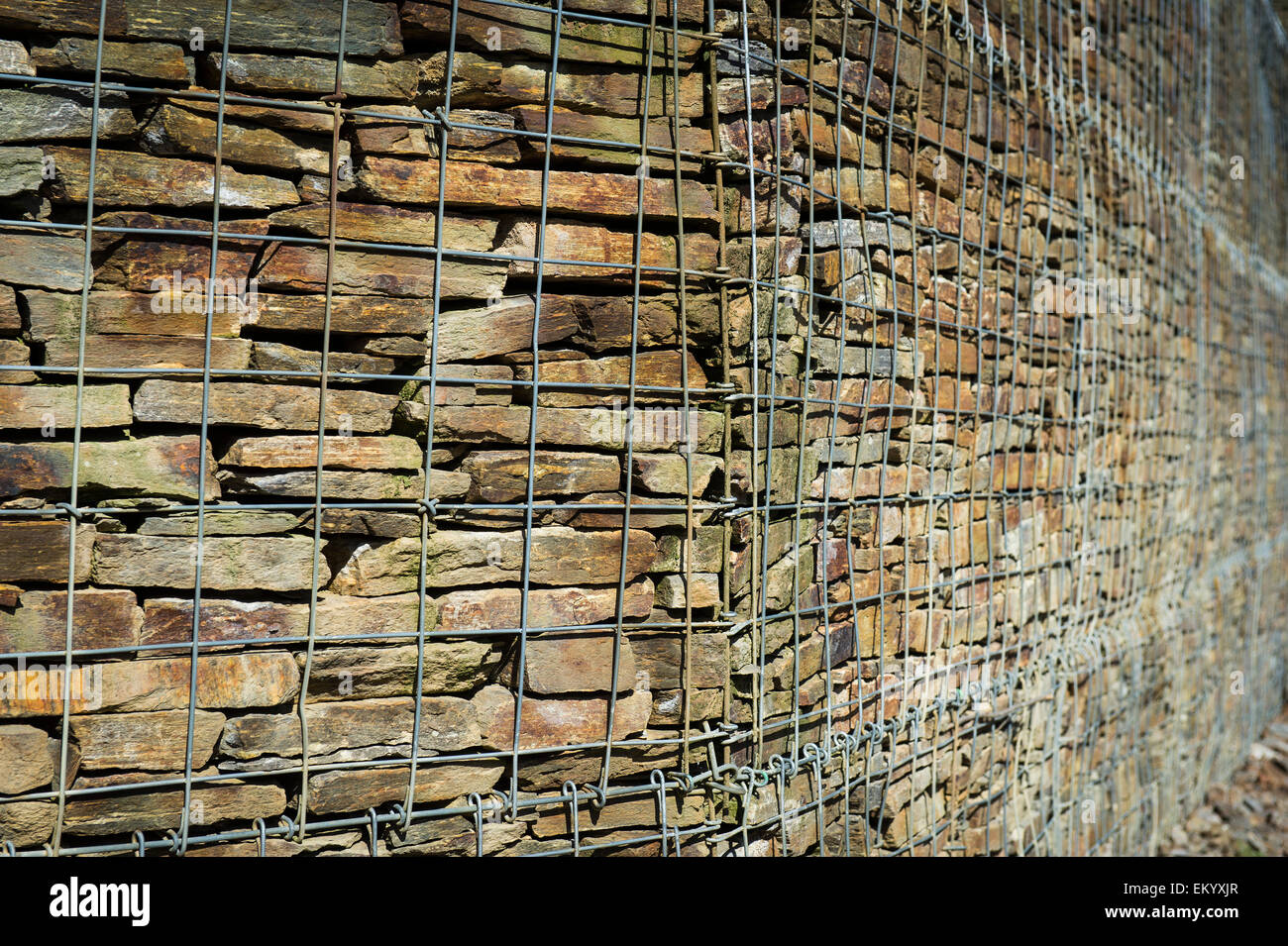Wall with stacked stones behind steel mesh Stock Photo - Alamy