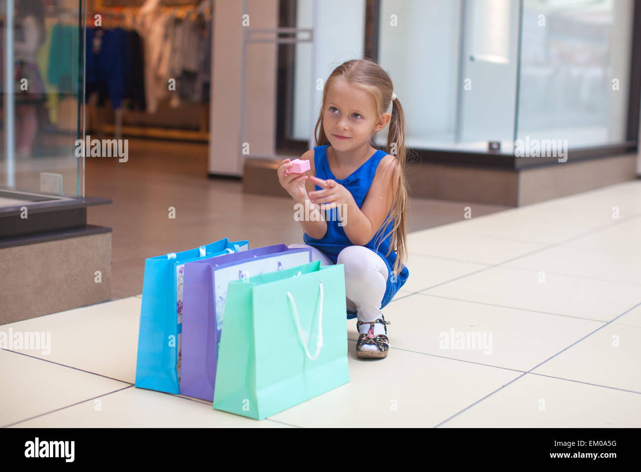 Little fashion girl sits near packages in a large shopping center Stock ...