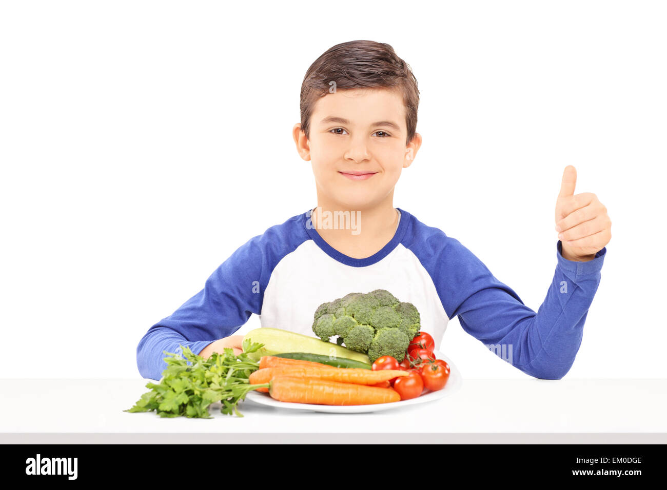 Little kid sitting on a table with a plate full of fresh vegetables and ...