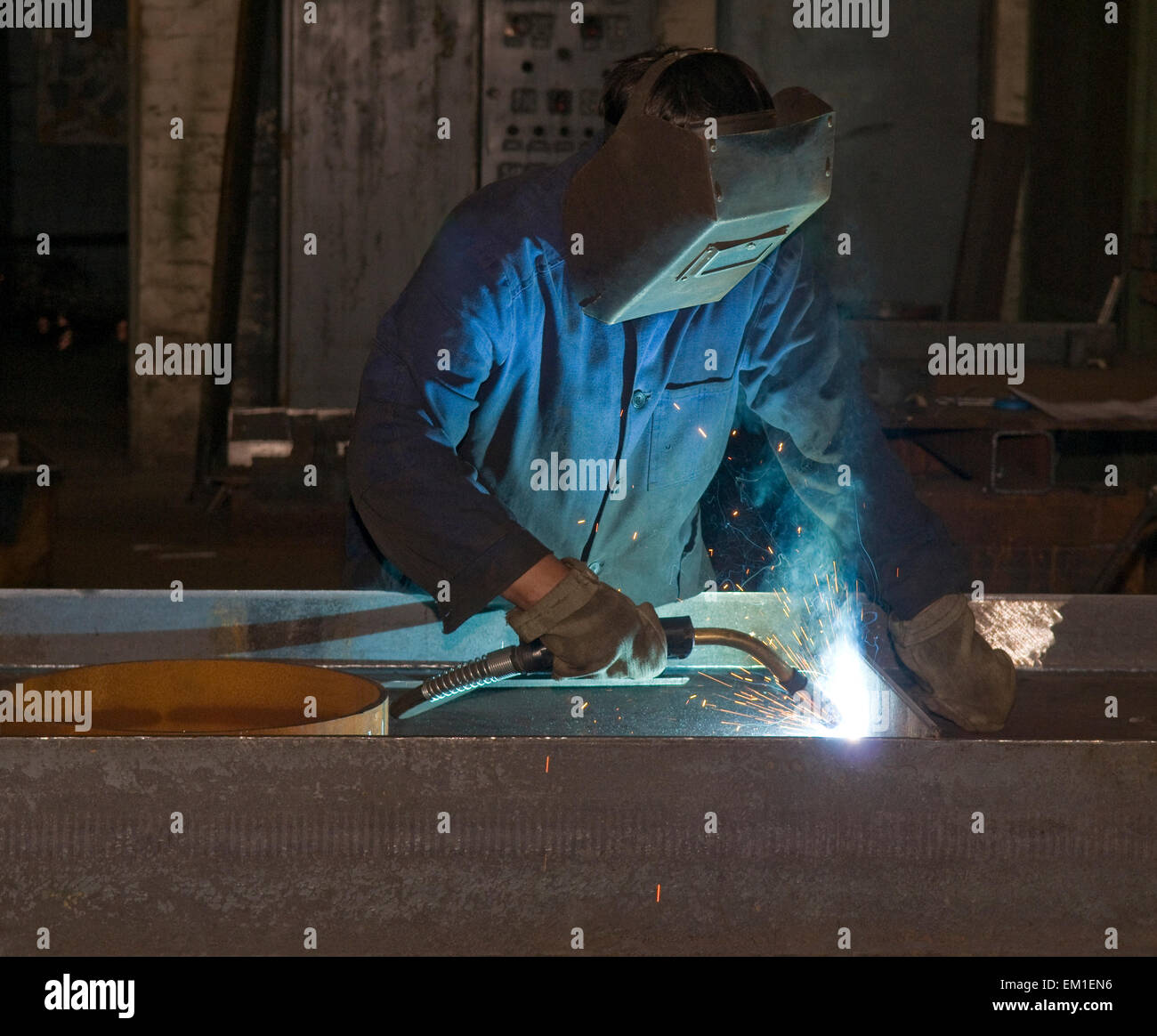 Working man with helmet shield on his head is welding steel ...