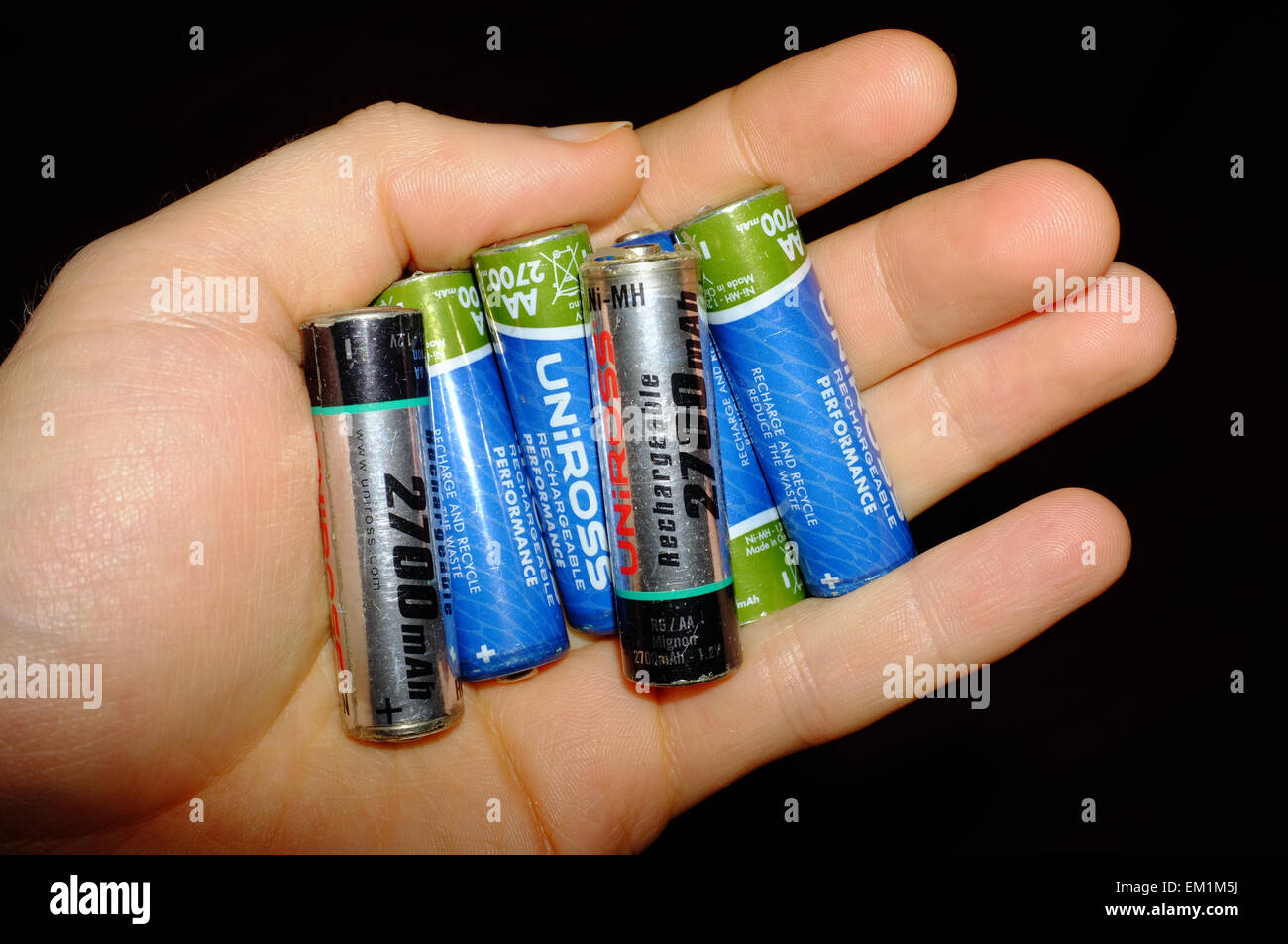 A white hand holding a AA rechargeable batteries against a black ...