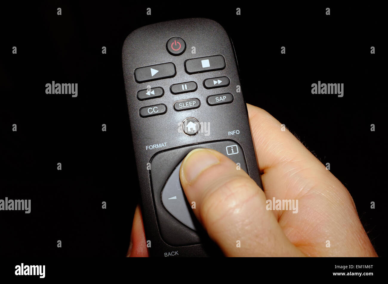 A white hand holding a TV remote control against a black background ...