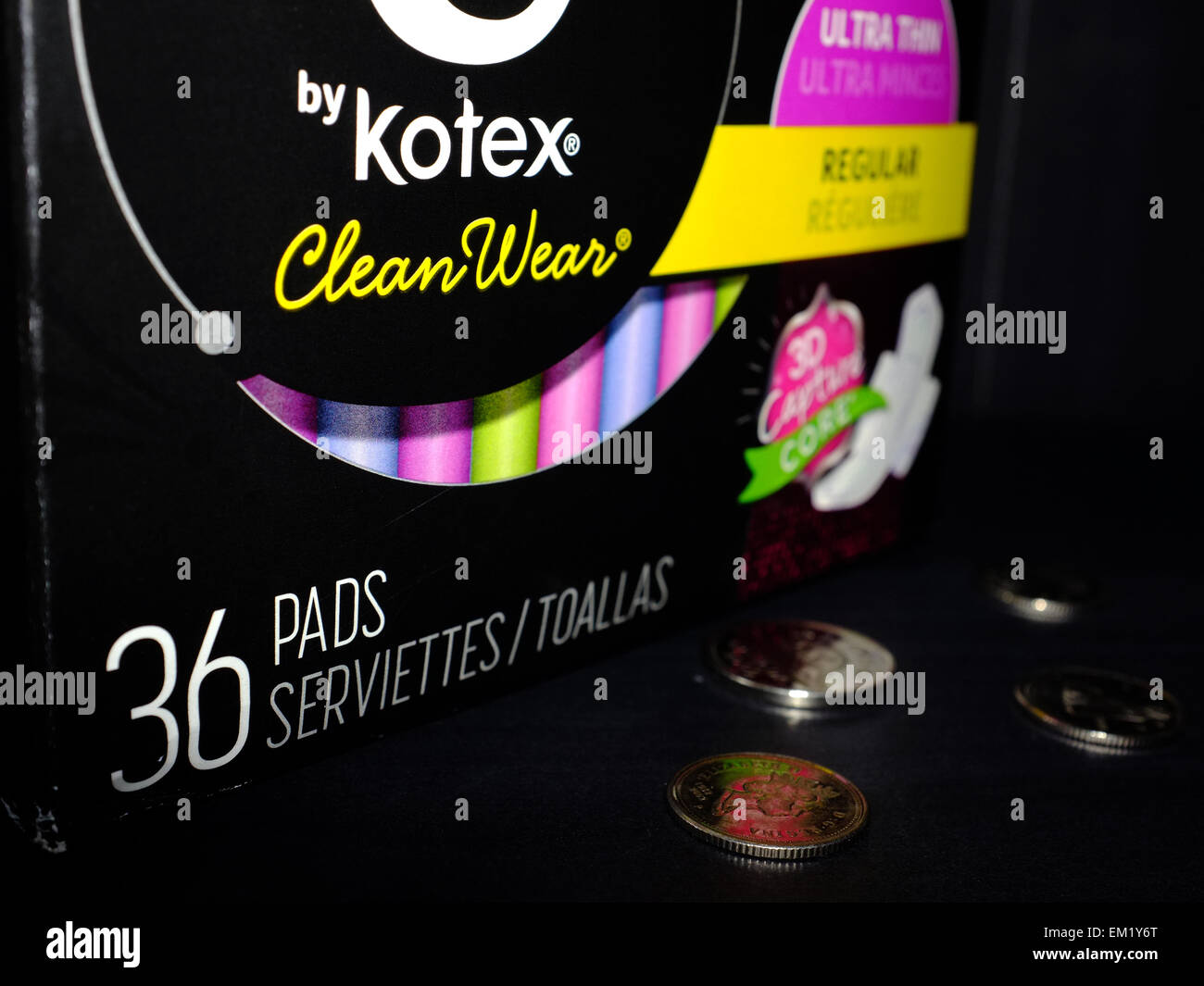 A packet of thin sanitary pads with coins photographed against a black ...