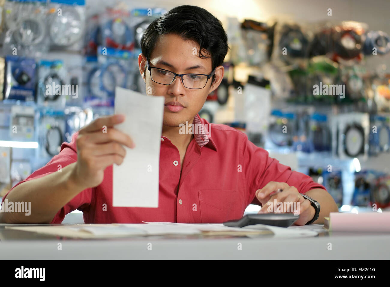 Young asian entrepreneur owning a computer shop and checking bills and ...