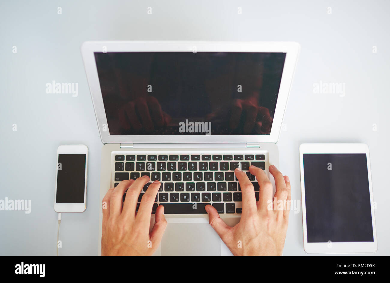 Human hands typing on laptop keypad between smartphone and digital ...