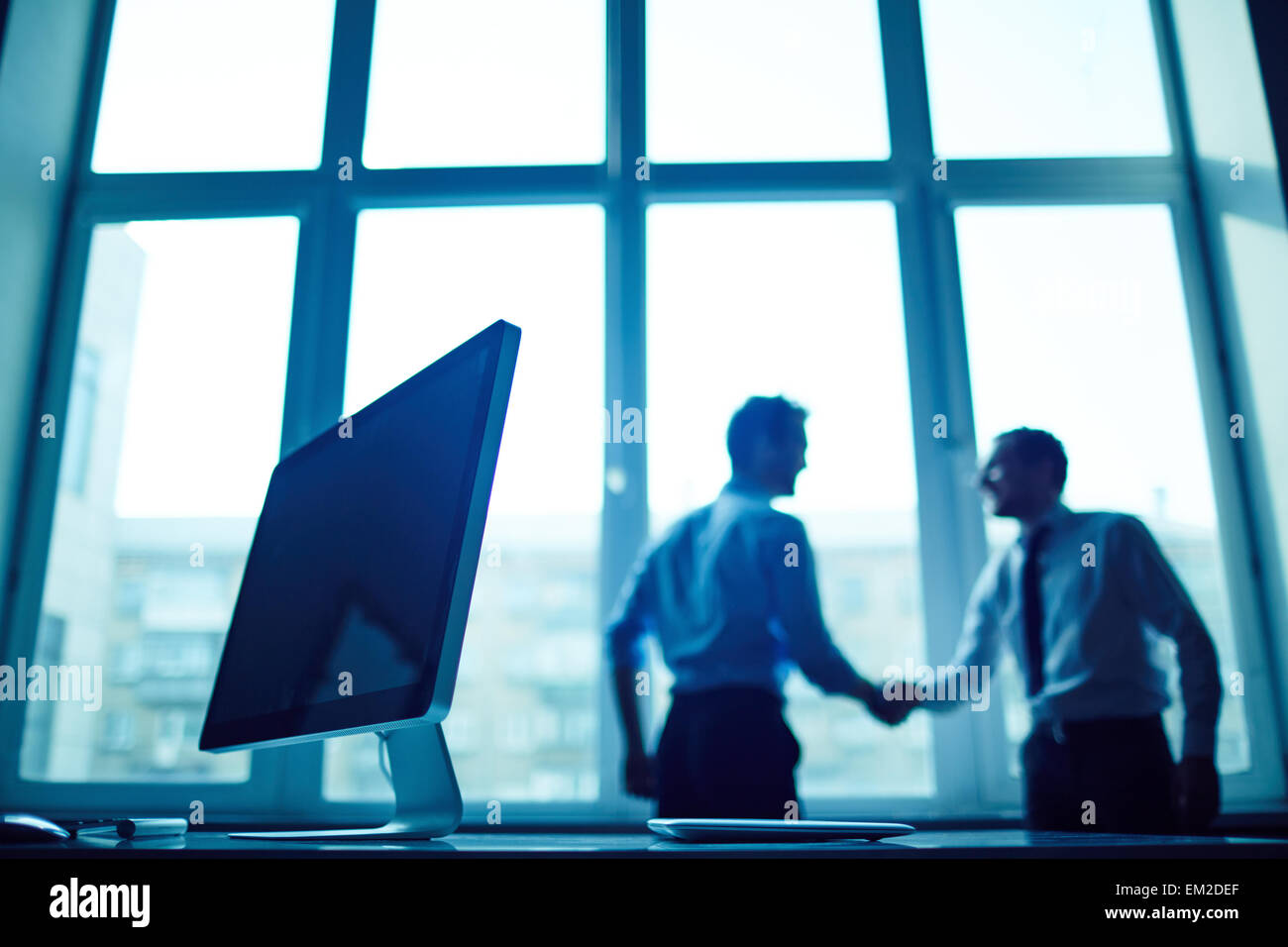 Computer monitor at workplace with two handshaking businessmen on ...