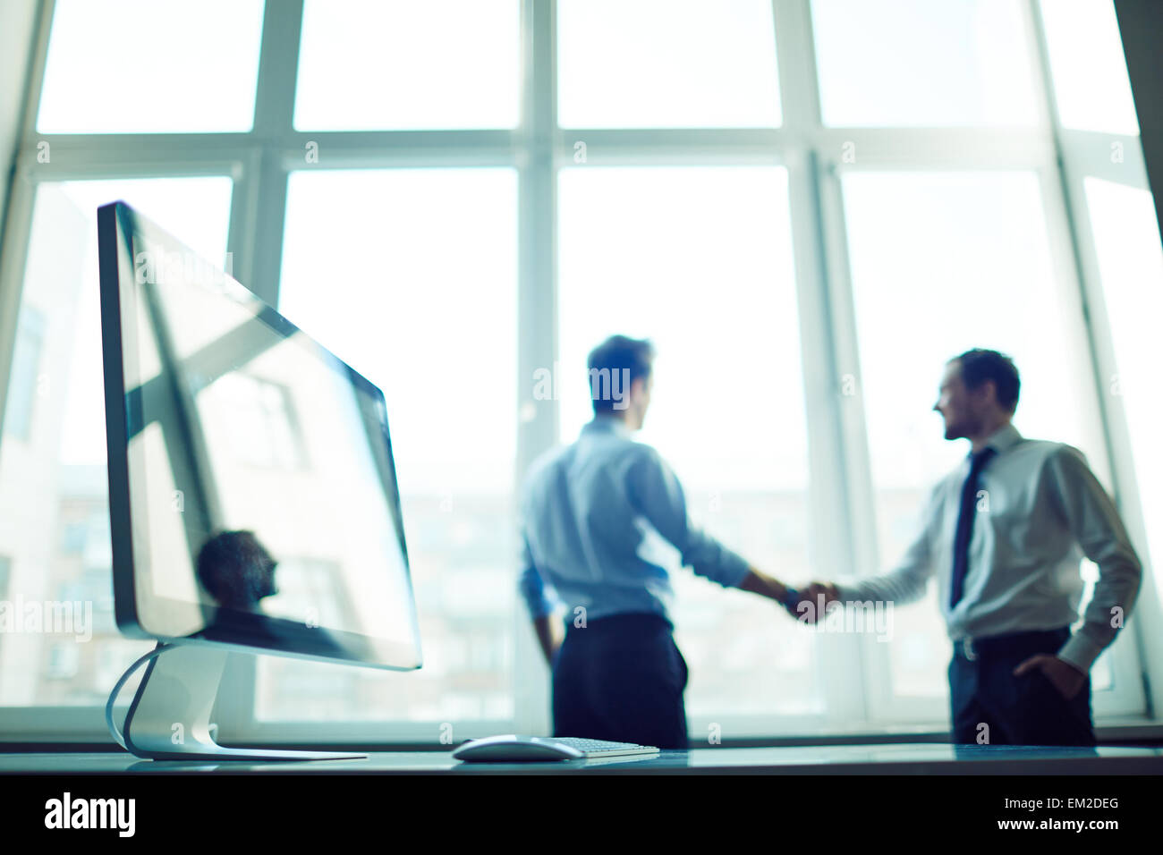 Computer monitor at workplace with two male colleagues handshaking on ...
