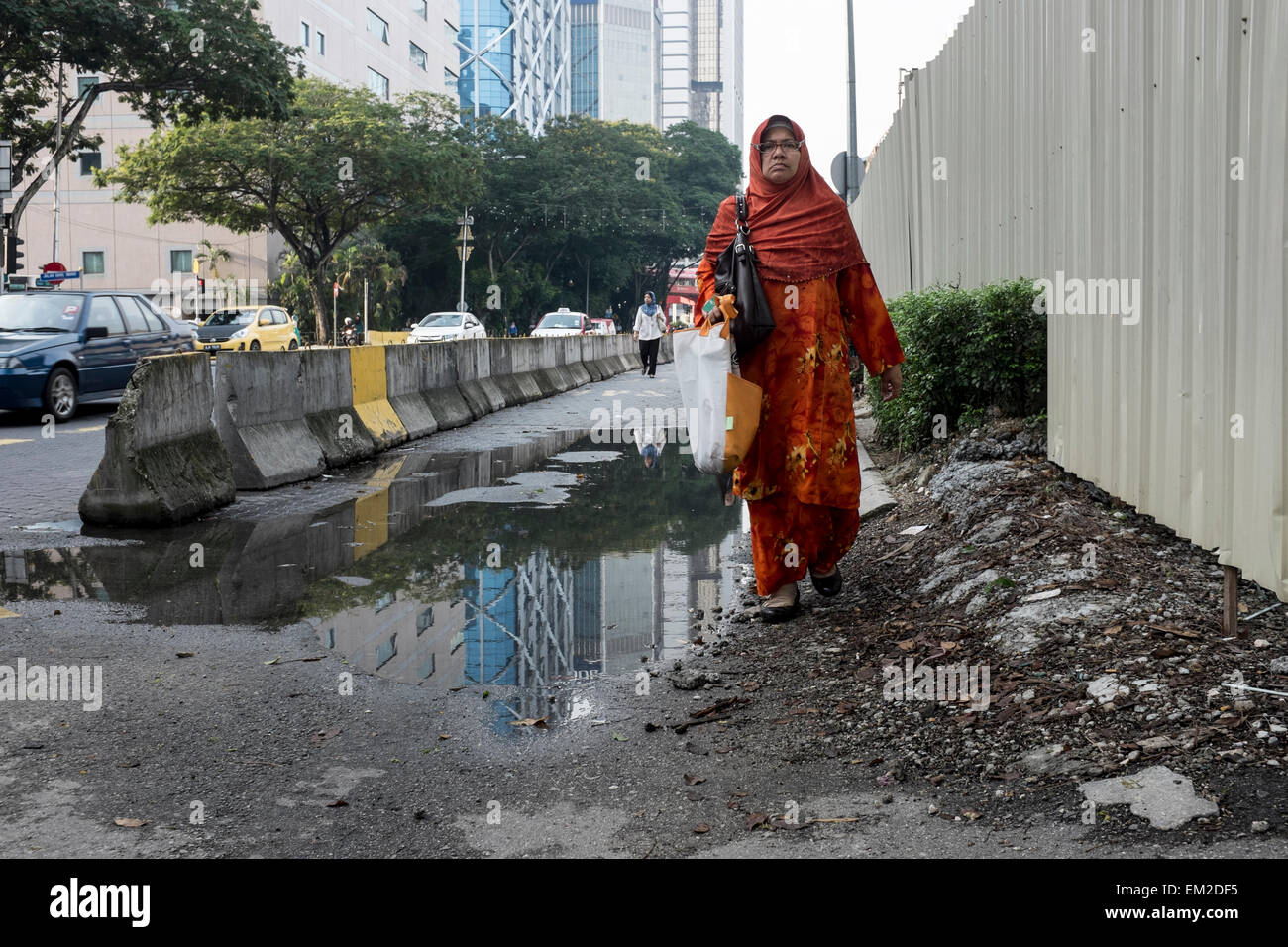 A Malaysian woman avoids a large puddle on the street as the walk to ...