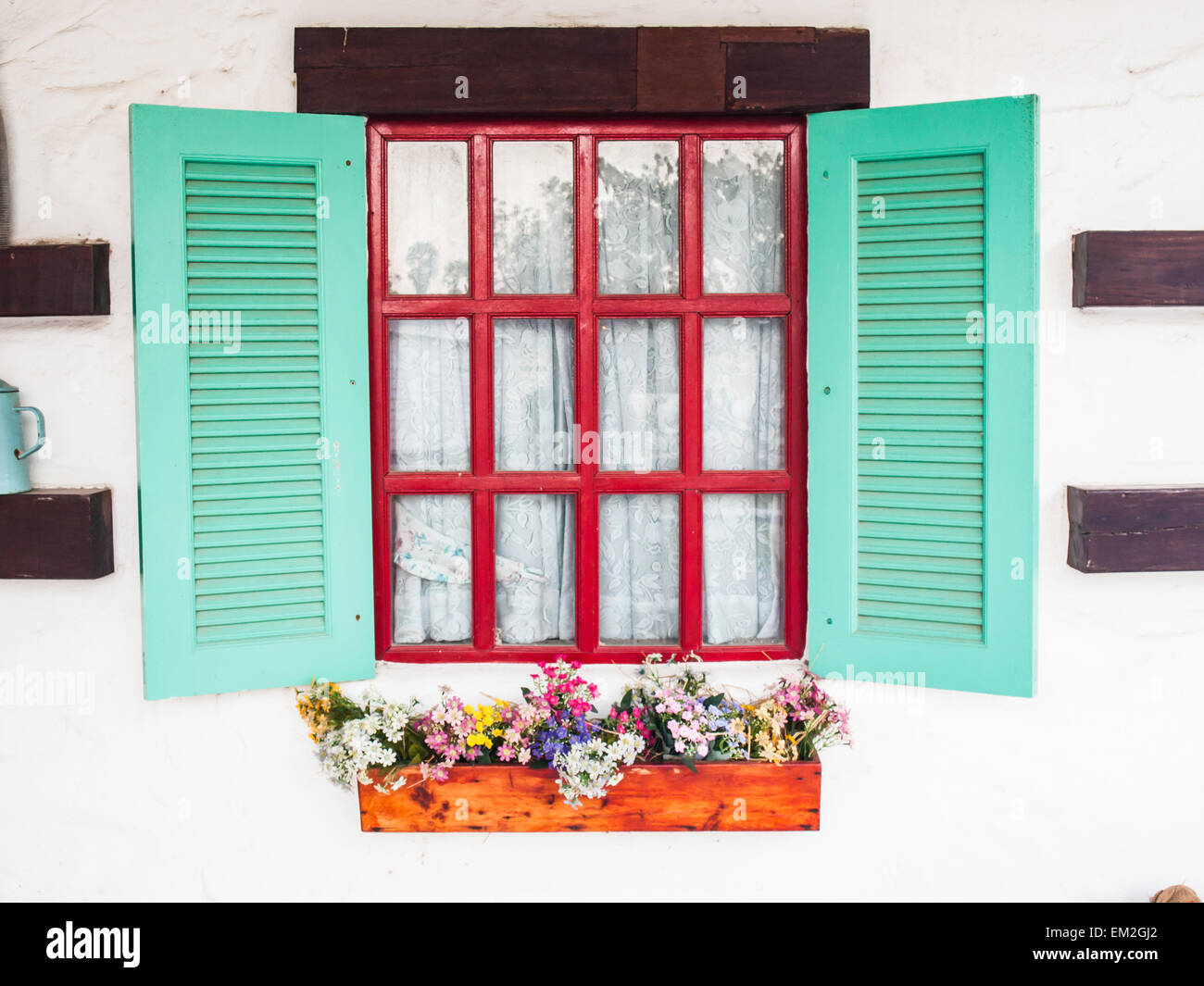 opened wooden shutter light green window on white wall with flower bed ...