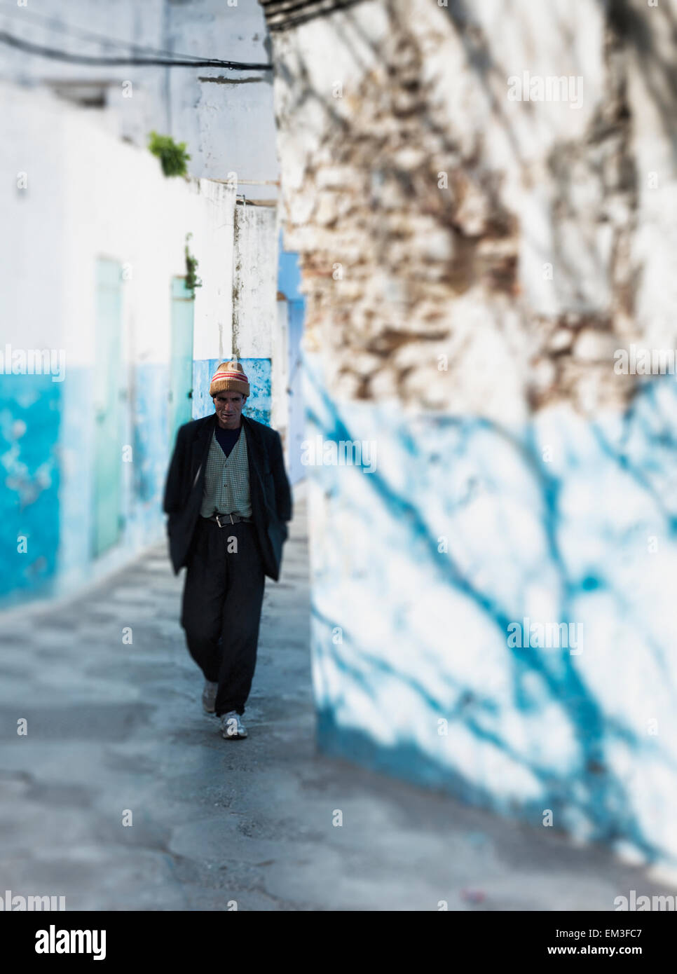 A Man Walking Down An Alleyway Between Buildings; Asilah Morocco Stock ...