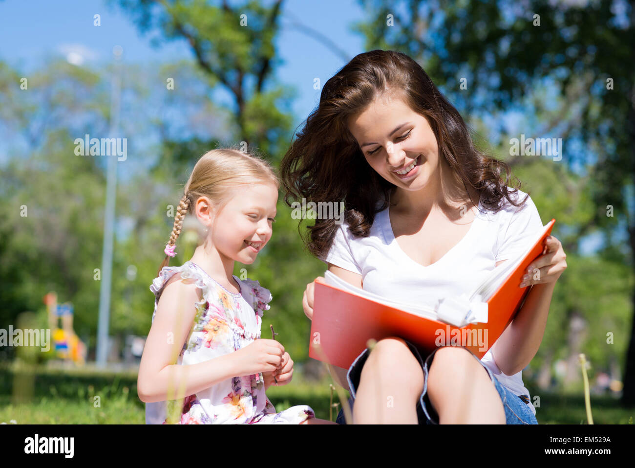 girl and a young woman reading a book together Stock Photo - Alamy