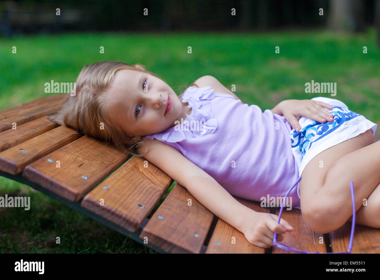 Cute little girl lying on wooden chair outdoor in the park Stock Photo ...