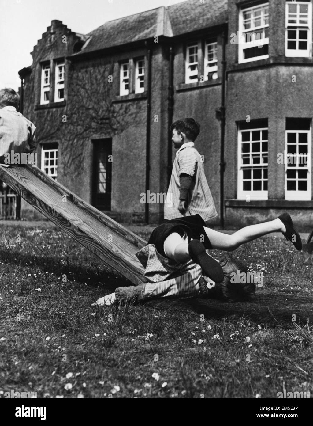 Two young boys playing on the slide in the garden, one comes flying off ...