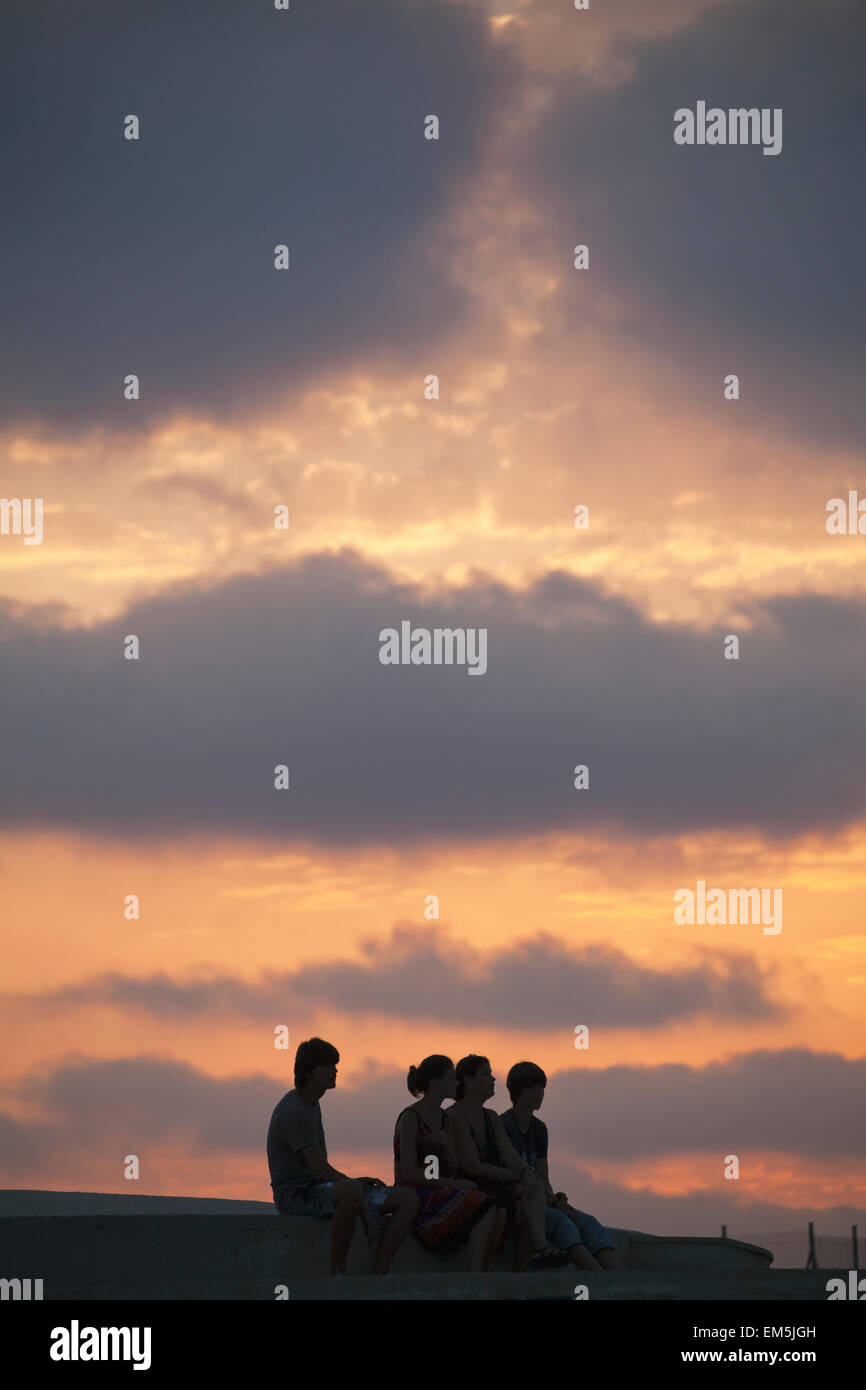 Cyprus, Paphos, Four people sitting on ledge at sunset Stock Photo - Alamy
