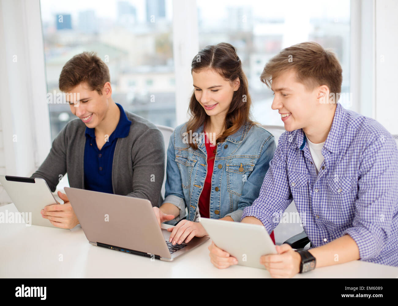 three smiling students with laptop and tablet pc Stock Photo - Alamy