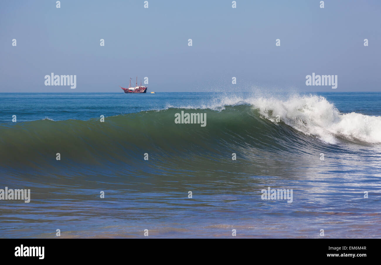 Mexico, Wave crashing close to shore with ship in distance; Puerto ...