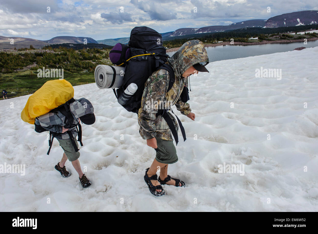 Boys cross a snowfield above Five Point Lake during a backpack trip ...