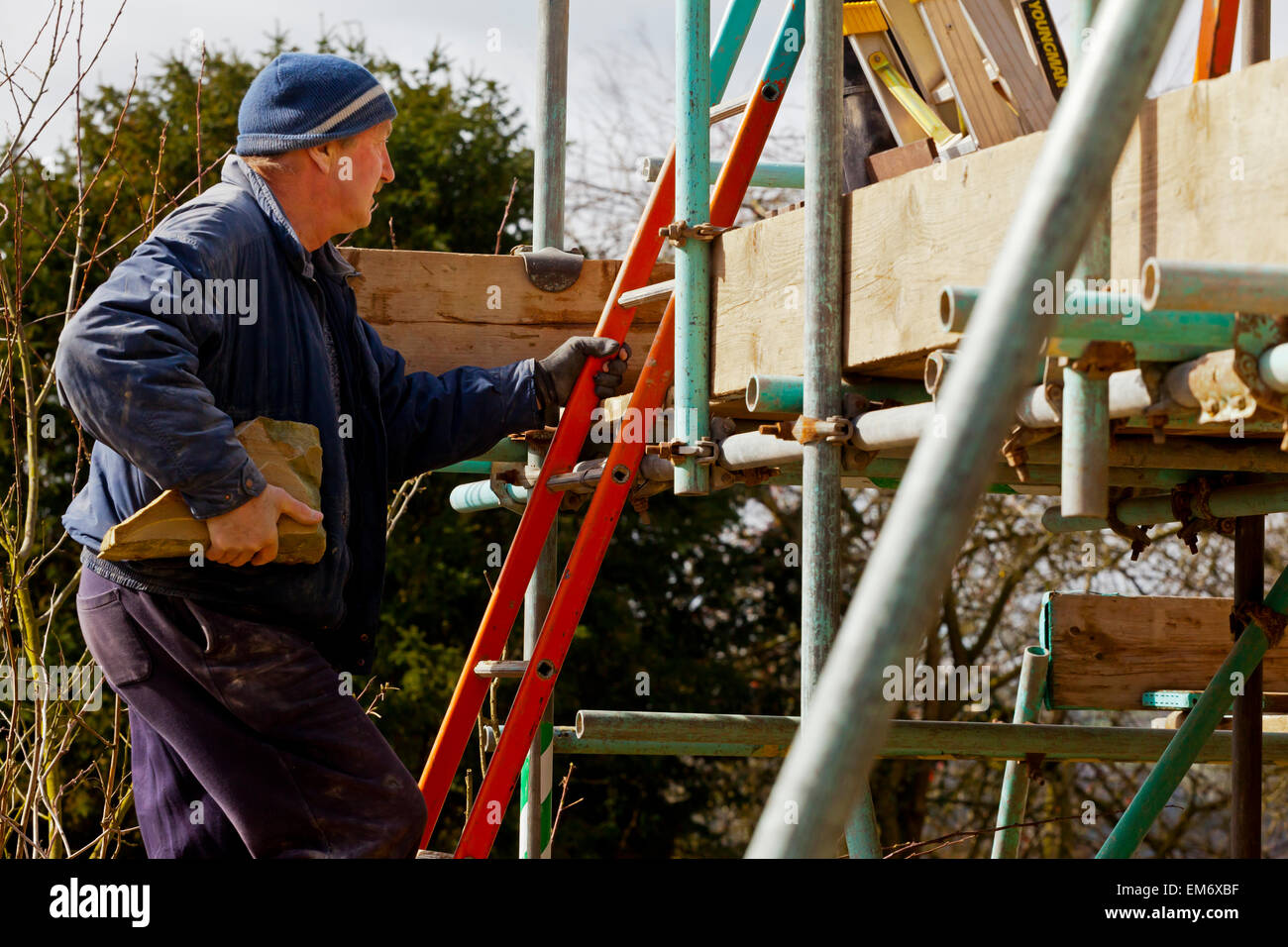 Builder on a ladder working on a construction site with scaffolding ...