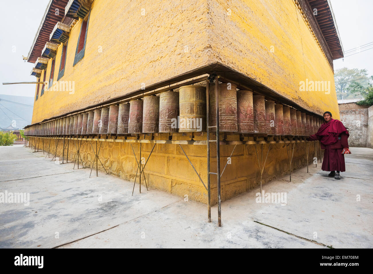 Buddhist temple wall with prayer wheels and a praying monk at Longwu ...
