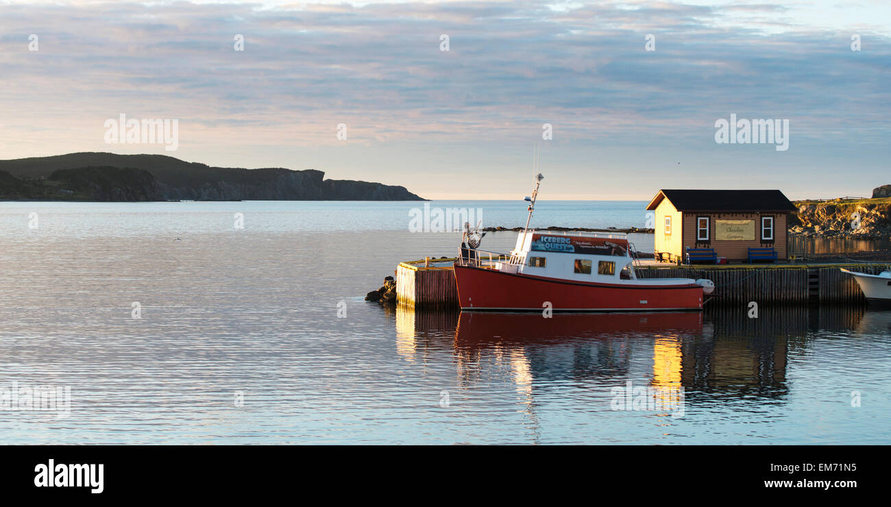 A small fishing boat sits on the tranquil water beside a pier ...