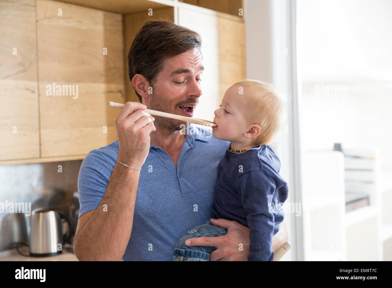 Man feeding toddler son with wooden spoon in kitchen Stock Photo - Alamy