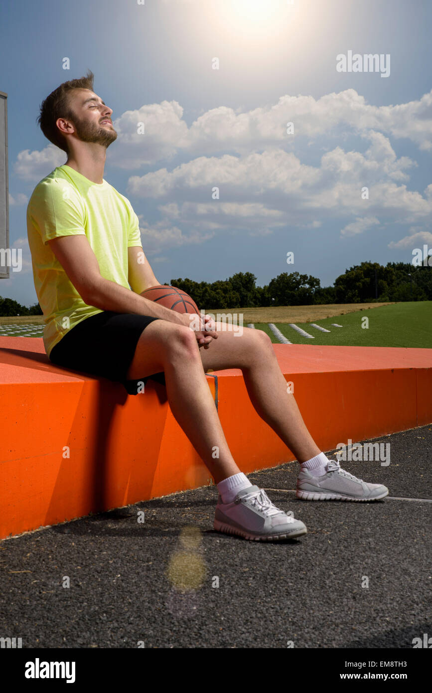 Young male basketball player sitting on wall taking a break Stock Photo ...