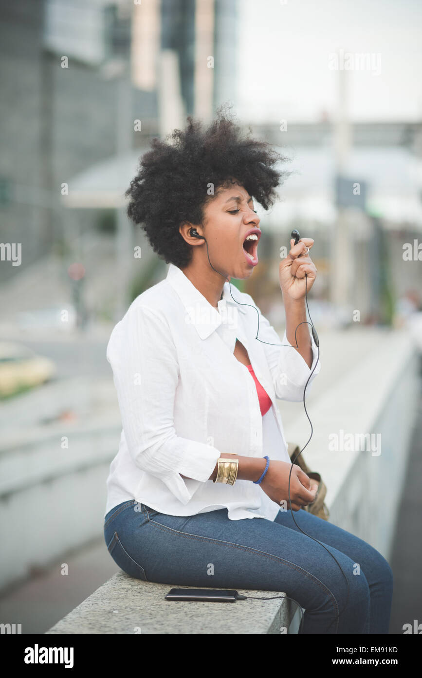 Young woman singing into earphone whilst sitting on shopping center ...