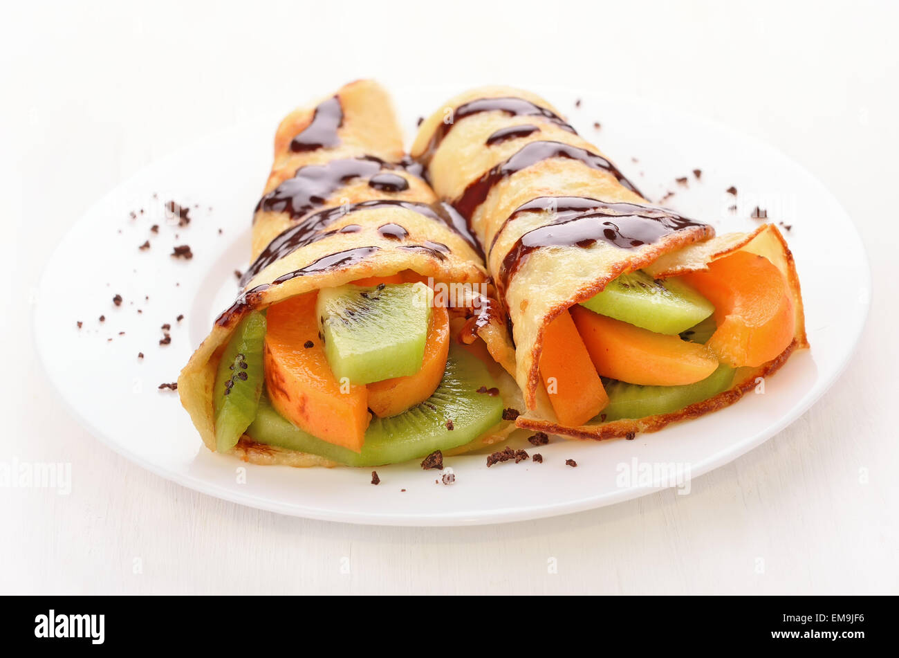 Crepes with fruit slices on white plate over wooden table Stock Photo ...