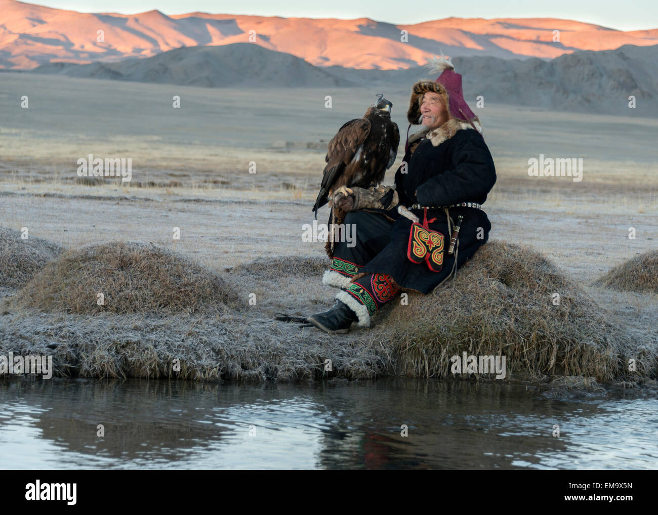 Elder eagle trainer resting by a stream with his golden eagle, Western ...