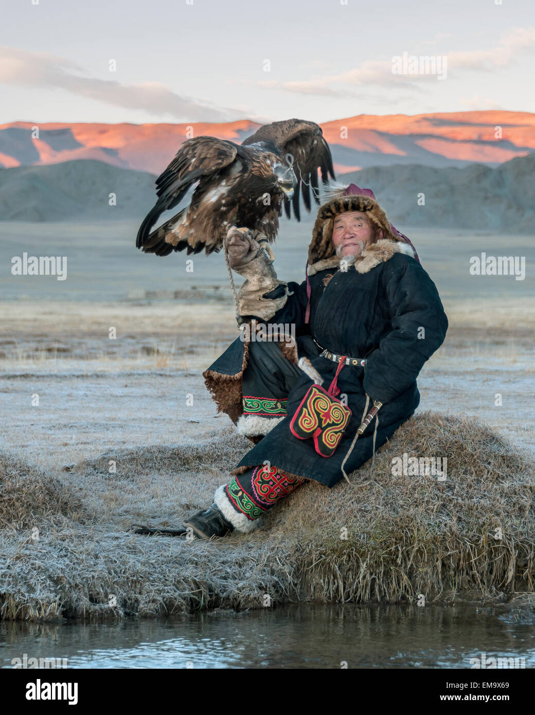 Elder eagle trainer by a stream with his golden eagle at sunrise ...