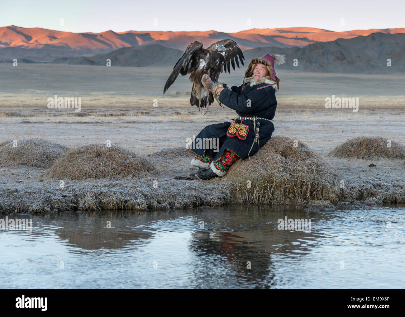 Elder eagle trainer by a stream with his golden eagle at sunrise ...