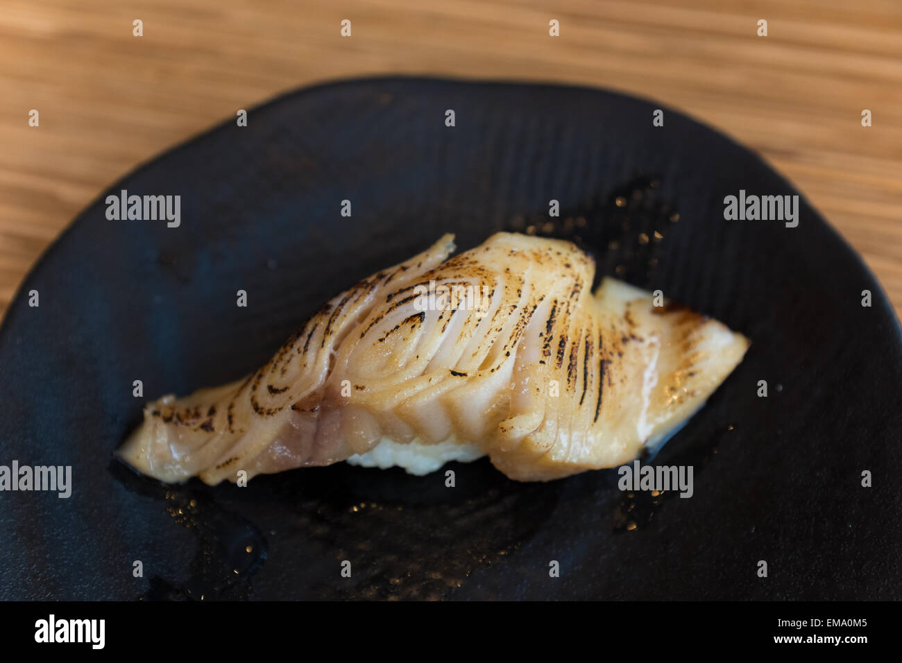 A piece of Sable fish sushi on a black plate Stock Photo - Alamy