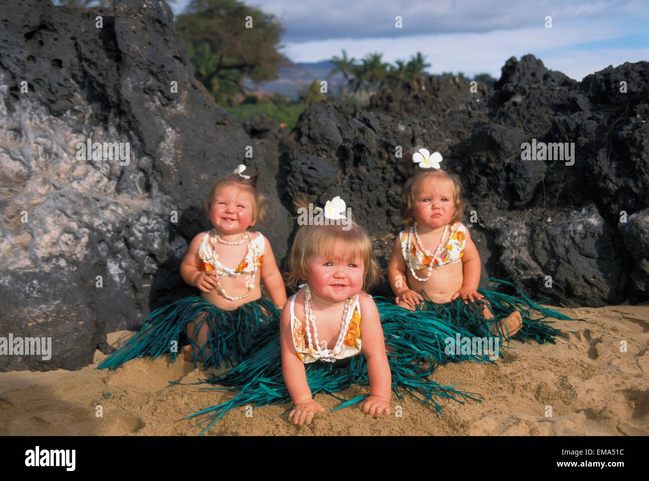 Three Babies Wearing Hula Sitting On Sand With Tropical Rock Background ...
