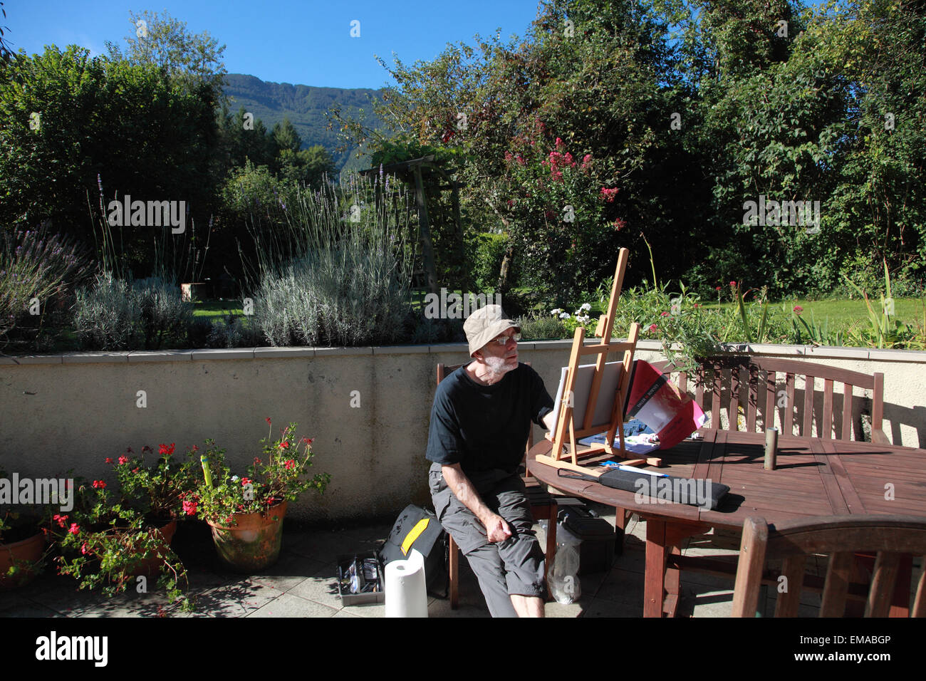 A retired man relaxing by painting in the sunshine in a garden in ...
