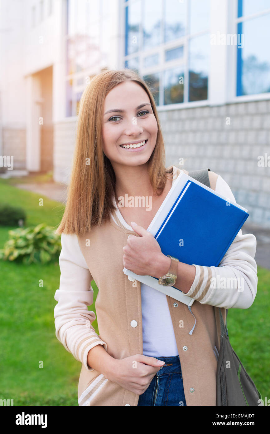 Student standing with books in her hands and smiling at camera on the ...