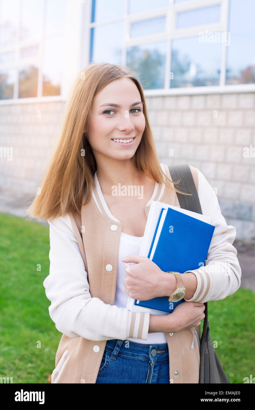 Student standing with books in her hands on building background Stock ...