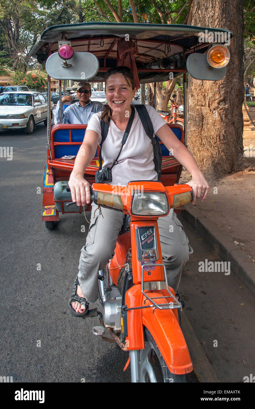White woman tourist smiling while driving an orange tuk tuk in Phnom ...