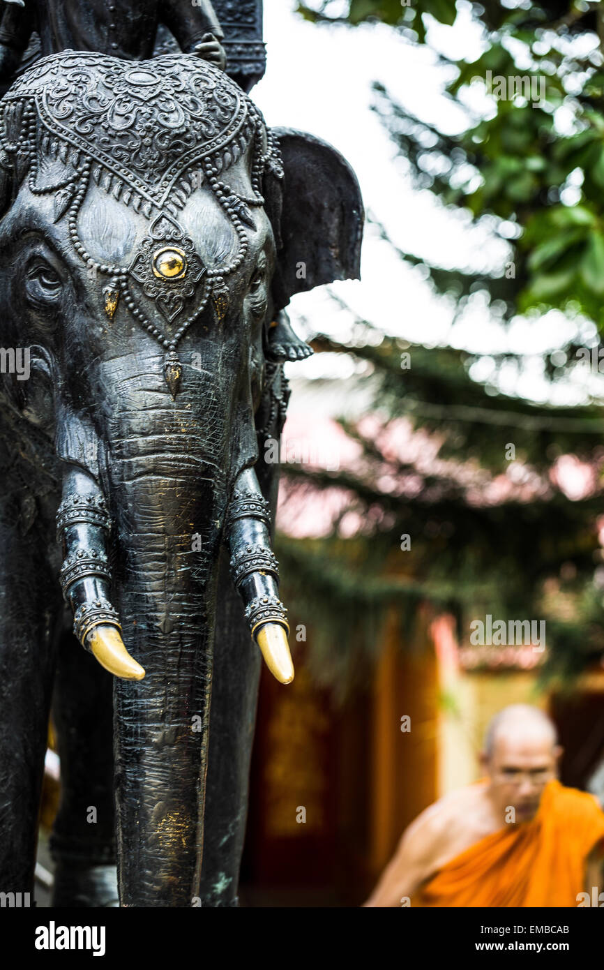 A Buddhist monk walks near to a statue of an elephant in a Buddhist ...