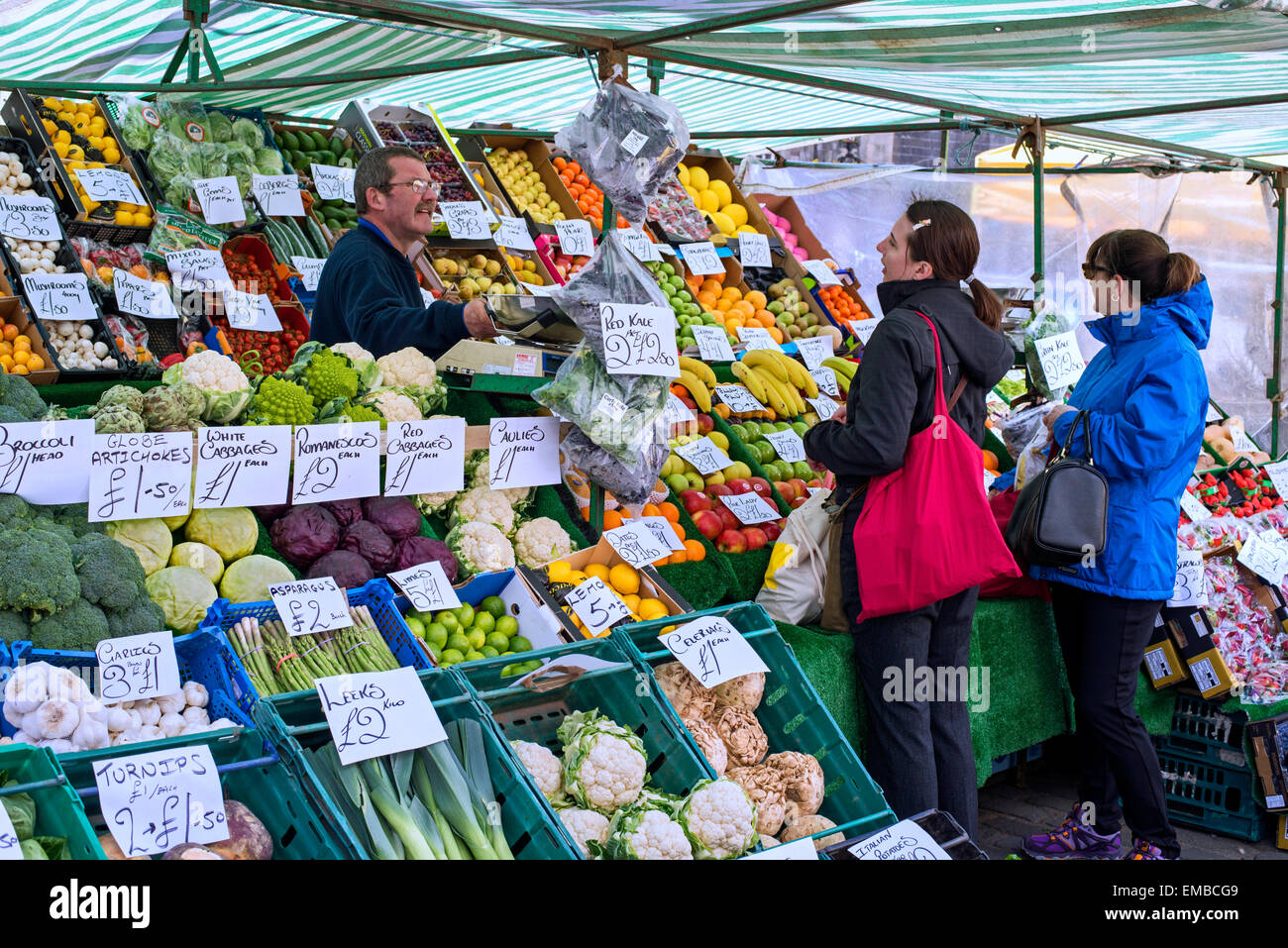 A stallholder serving customers at a fruit and veg stall in the ...