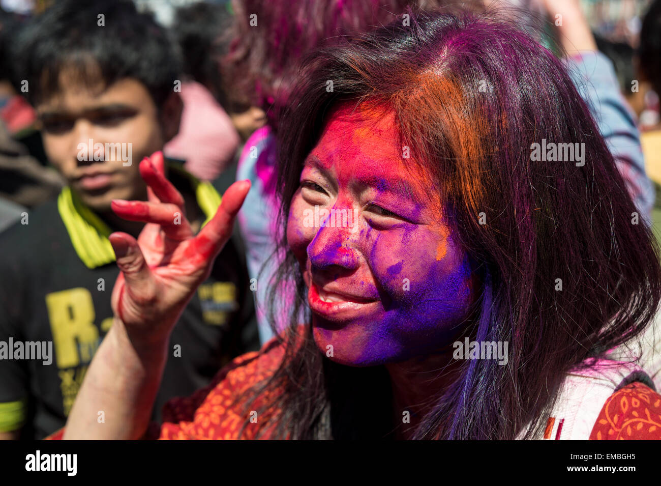 Asian woman with face painted in red waving at the camera during holi ...