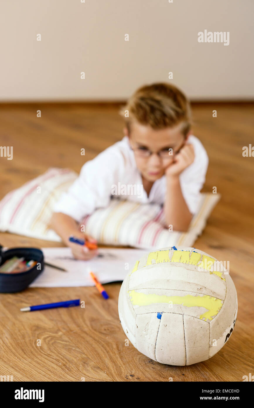 Boy doing homework on wooden floor with soccer ball lying in the ...